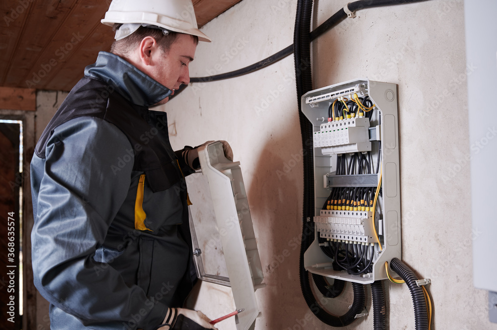 Electrical engineer in work uniform checking electric box with wires ...