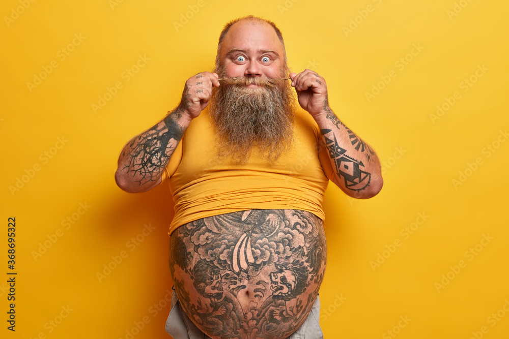 Horizontal shot of funny thick guy with big tummy, tattooes on arms and ...