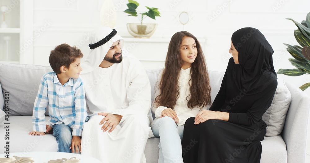 Portrait of cheeful Muslim family with two kids sitting on couch and ...