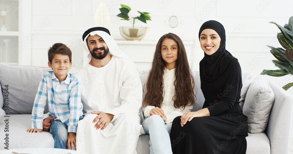 Portrait of cheeful Muslim family with two kids sitting on couch and ...