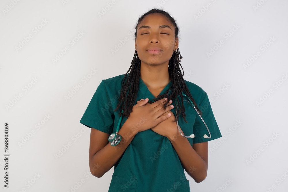 Faithful doctor woman closes eyes and keeps hands on chest near heart ...