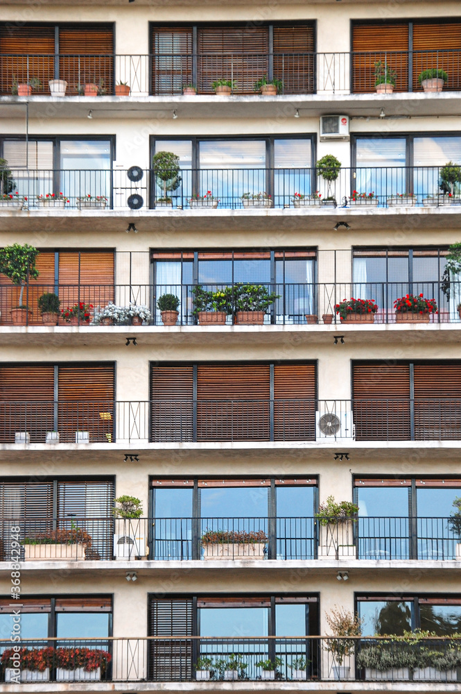 Balconies of a modern building with plants and shutters. City facade of ...