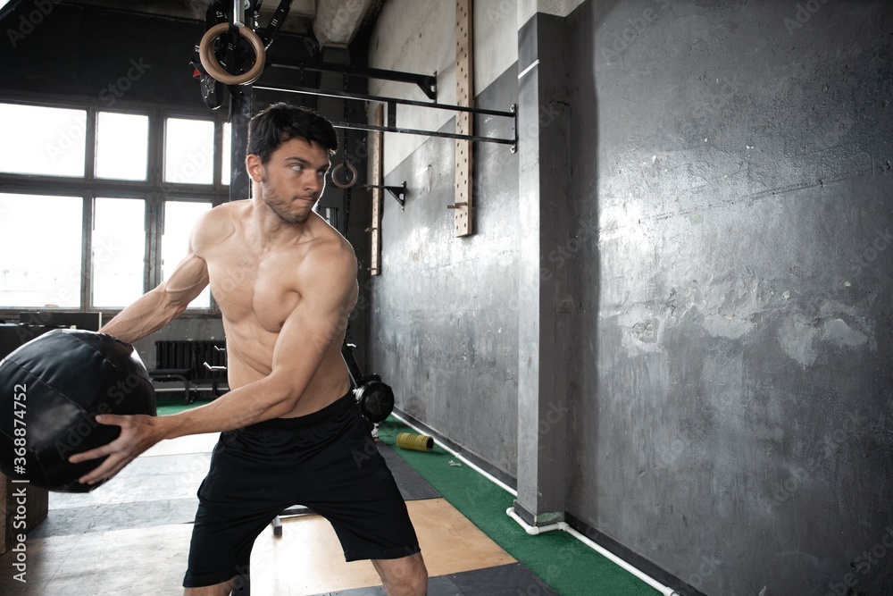 Young strong sweaty focused fit muscular man doing throwing medicine ...