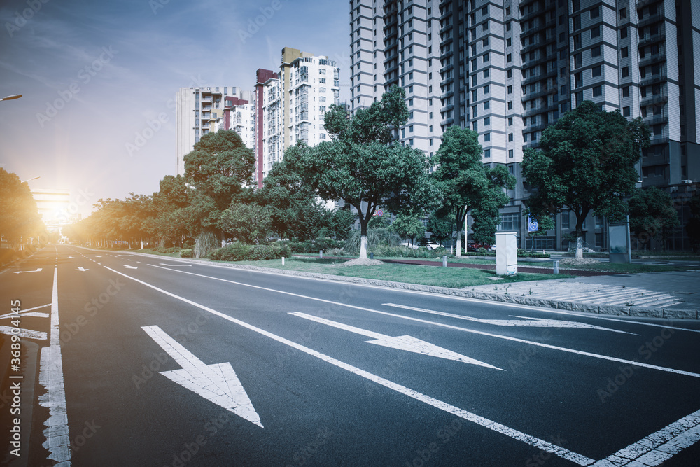 Clear sky, asphalt road with traffic guide lines beside high-rise ...