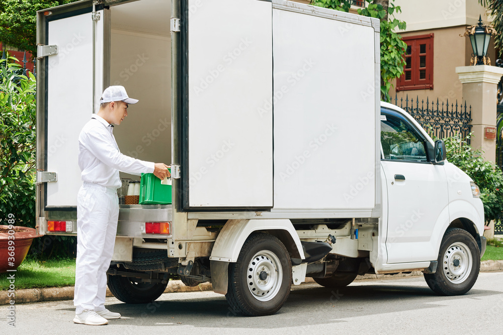 Delivery man in white uniform taking plastic crate with glass milk ...