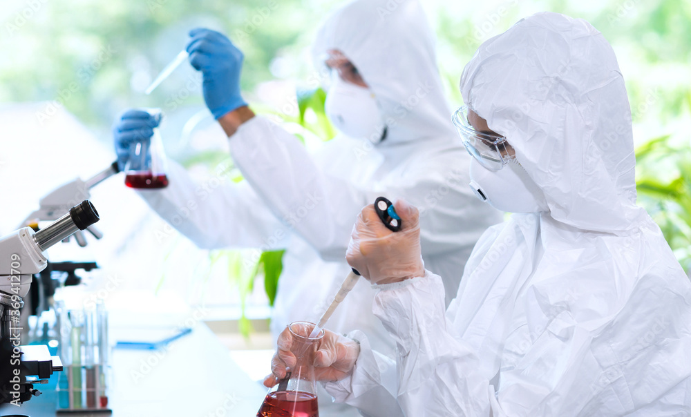 Scientists in protection suits and masks working in research lab using ...