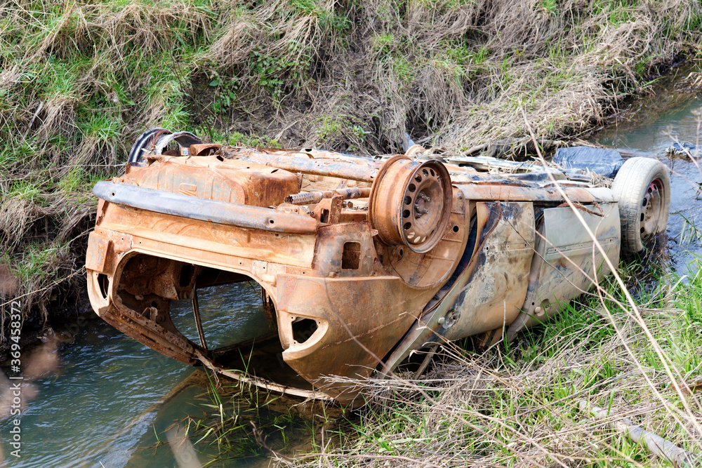 Stolen burnt rusty car abandoned in a river in a countriside polluting ...