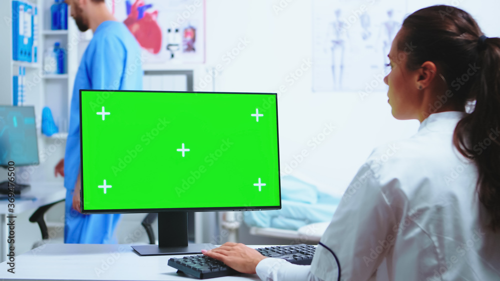 Physician writing diagnose on computer with green screen and assistant ...