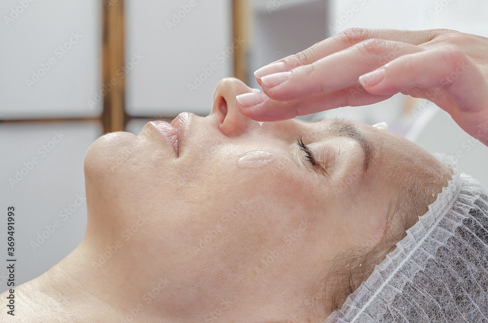 Beautician hand applies cream on face of woman in a spa salon. Relaxed ...