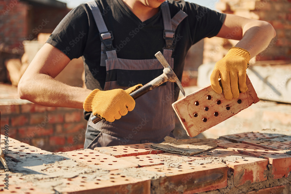 Holding brick and using hammer. Construction worker in uniform and ...