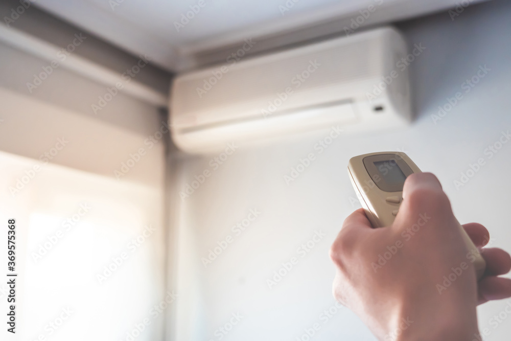 Hand with air conditioner remote control changing the home temperature ...