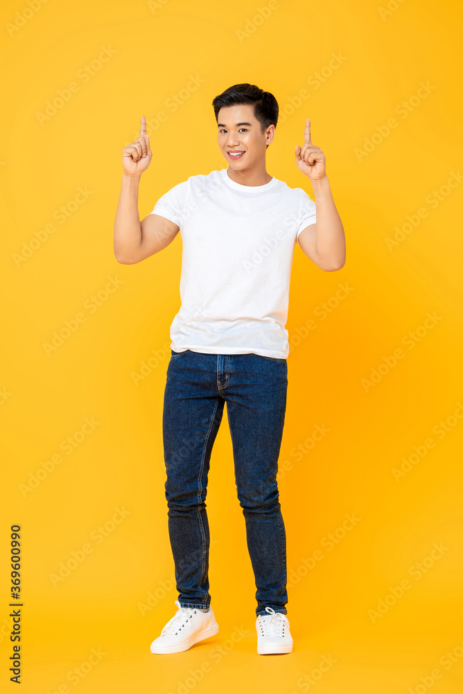 Smiling young handsome Asian man standing and pointing two fingers up ...