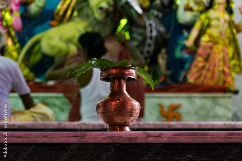 Red metallic lota with mango leaves on top in front of devi durga ...