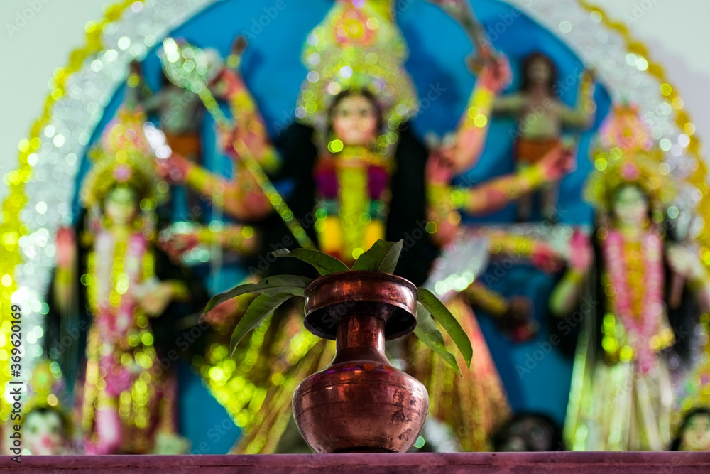 Red metallic lota with mango leaves on top in front of devi durga ...