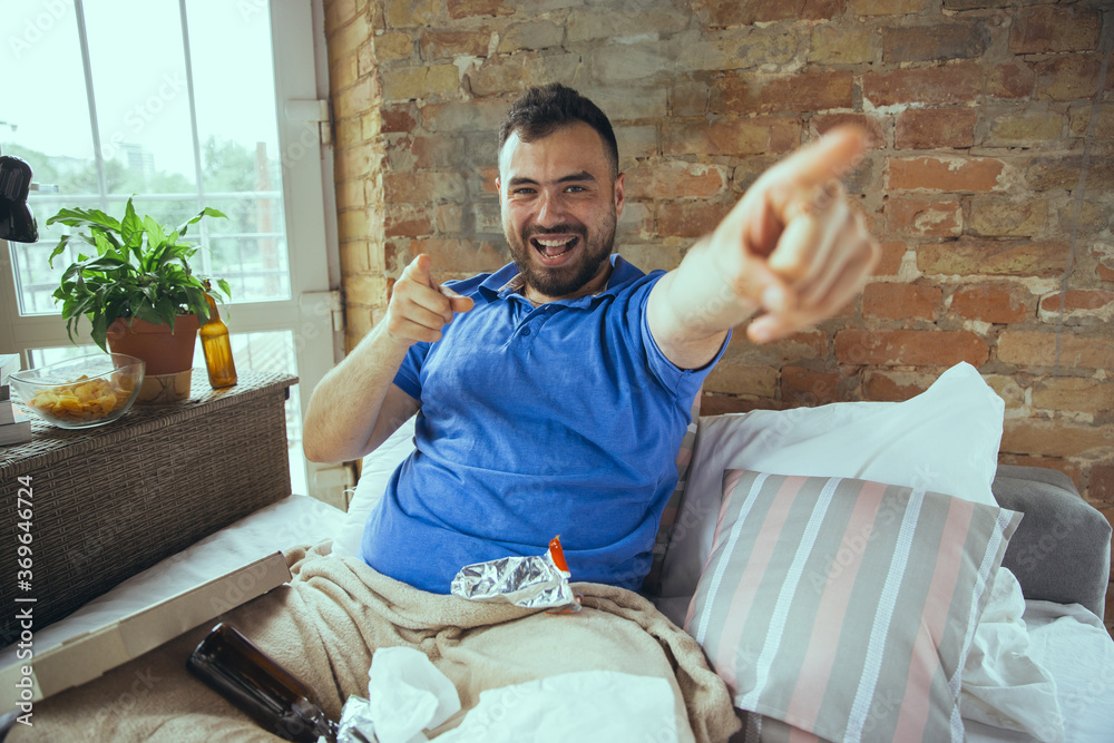 Pointing, laughting. Lazy caucasian man living in his bed surrounded ...