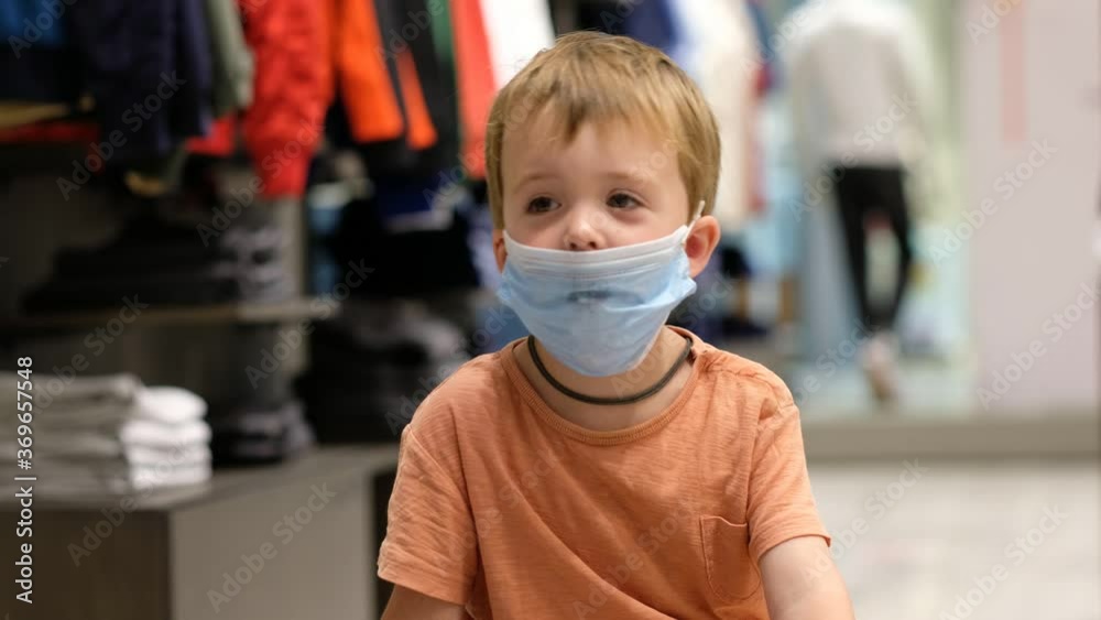 Kid boy in a protective medical mask sits and waits for parents while ...