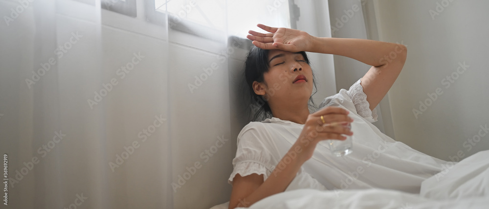 An Ill Woman Drinks Water And Consuming A Pill While Lying On The Bed