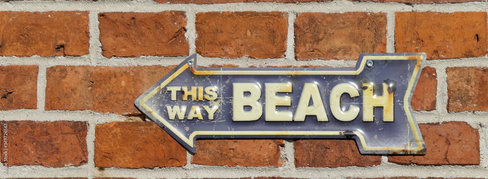 This way beach. Old rusty metal sign on a red brick wall. Blue with ...