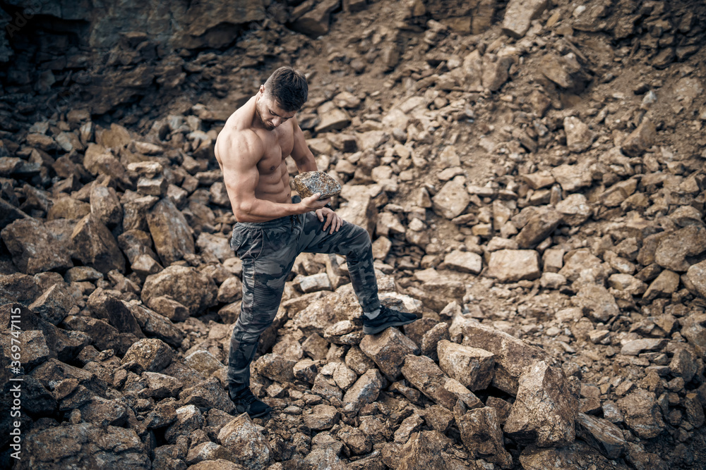 Full size photo of an athletic guy posing with rock in a quarry ...