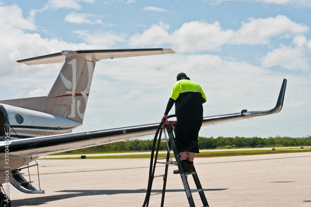 airport maintenance man on a ladder filling wing tank with aviation ...