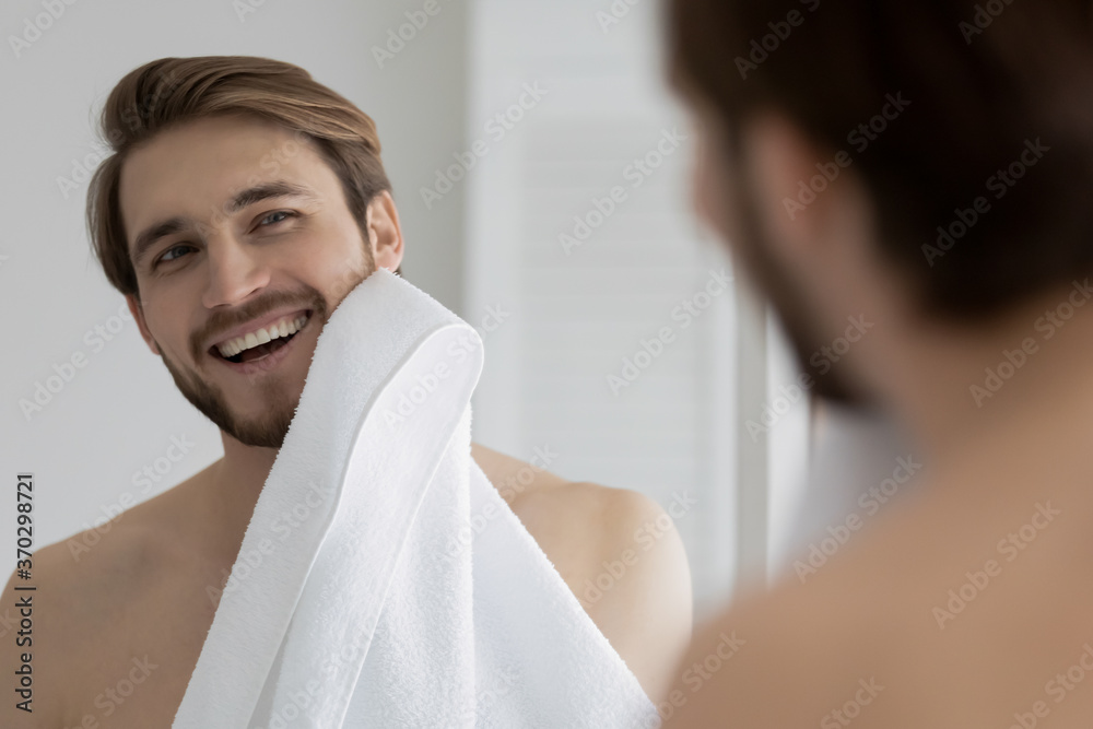 Mirror reflection smiling young man wiping face with white towel after ...