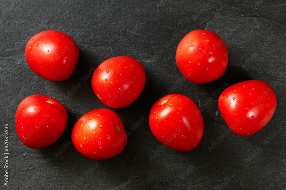 Top down view, seven mini tomatoes with drops of water on black stone ...