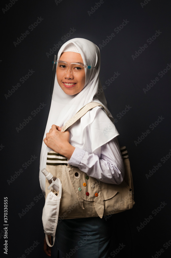 Indonesian Muslim high school student wearing face shield and bring mask, hand sanitizer and ...