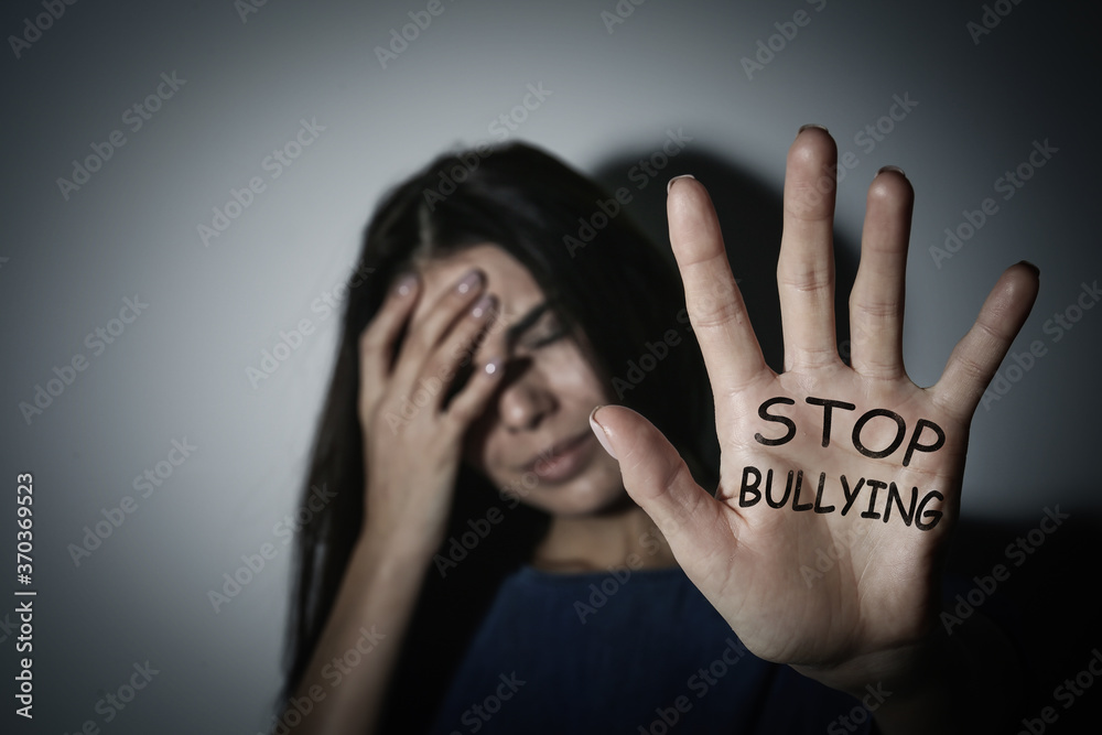 Crying teen girl showing palm with message STOP BULLYING near white ...