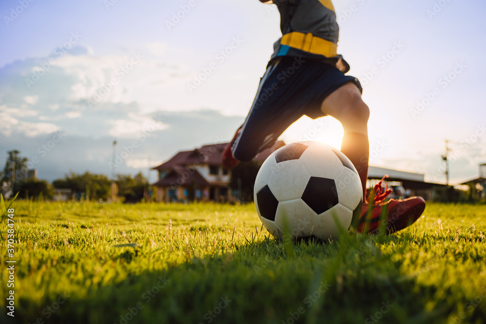 Boy kicking a ball while playing street soccer football on the green ...