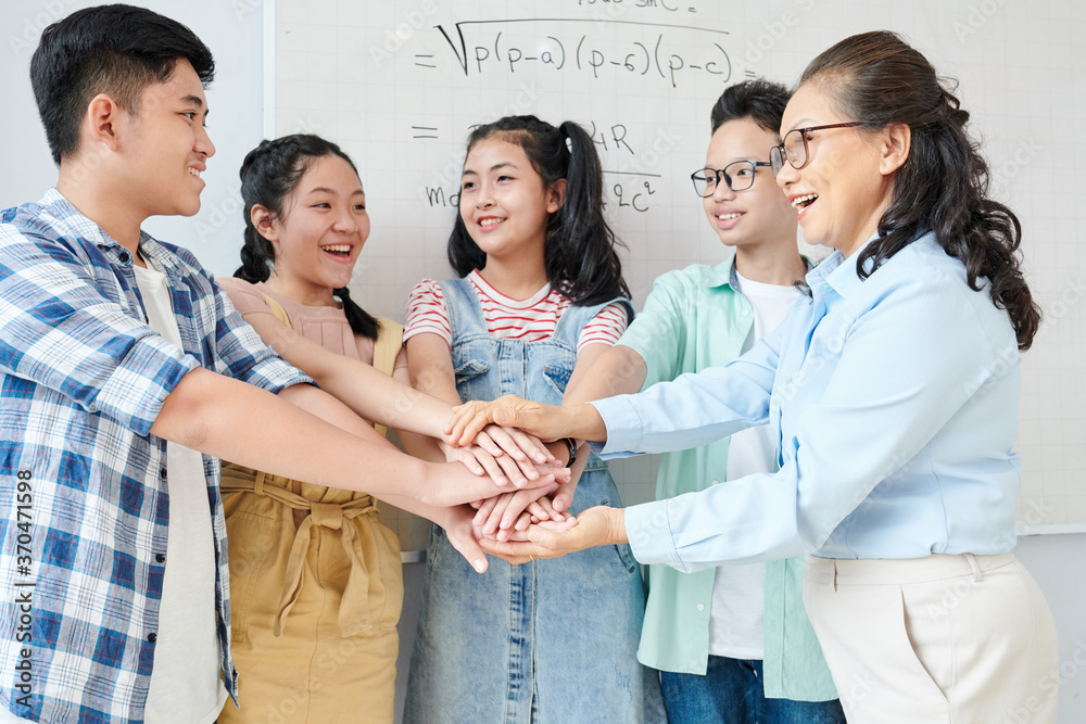 Group of students and their math teacher stacking hands to support each ...