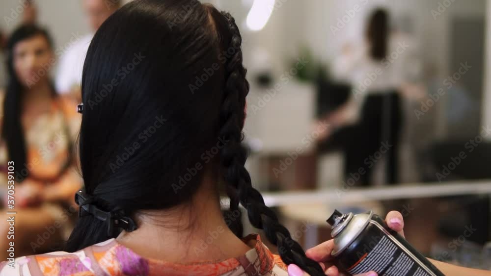 Female stylist applying hairspray fixing plaiting hairstyle on brunette ...