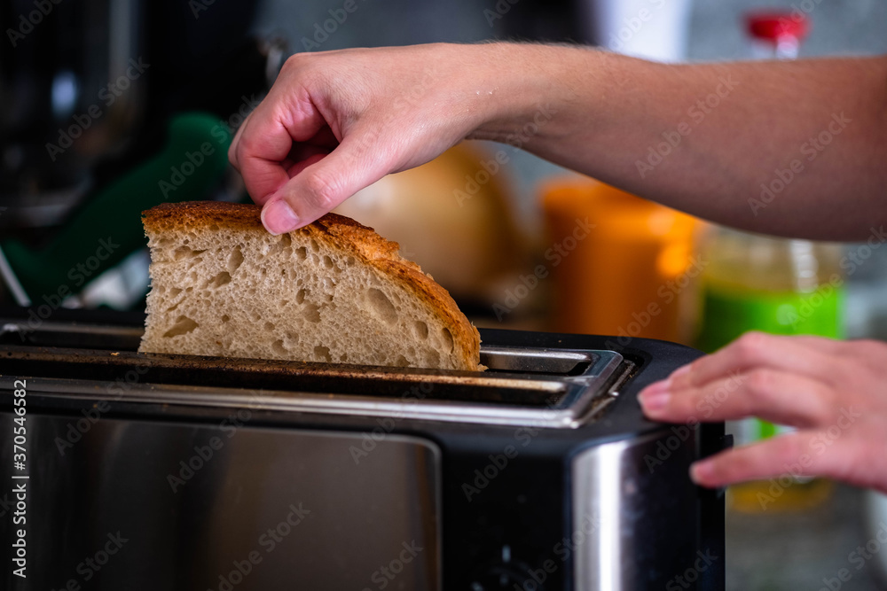 Female hand putting fresh whole wheat bread into toaster. Hands girl ...
