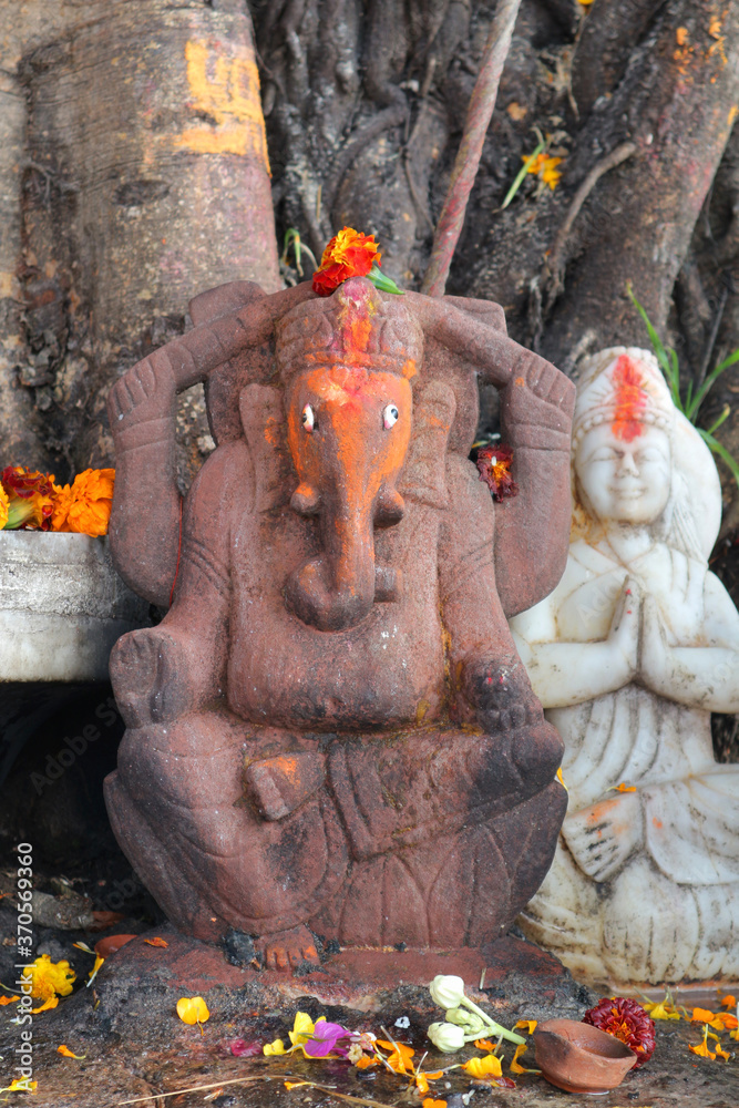 Stone deity of the Indian god Ganesh under a banyan tree. Hindu ...