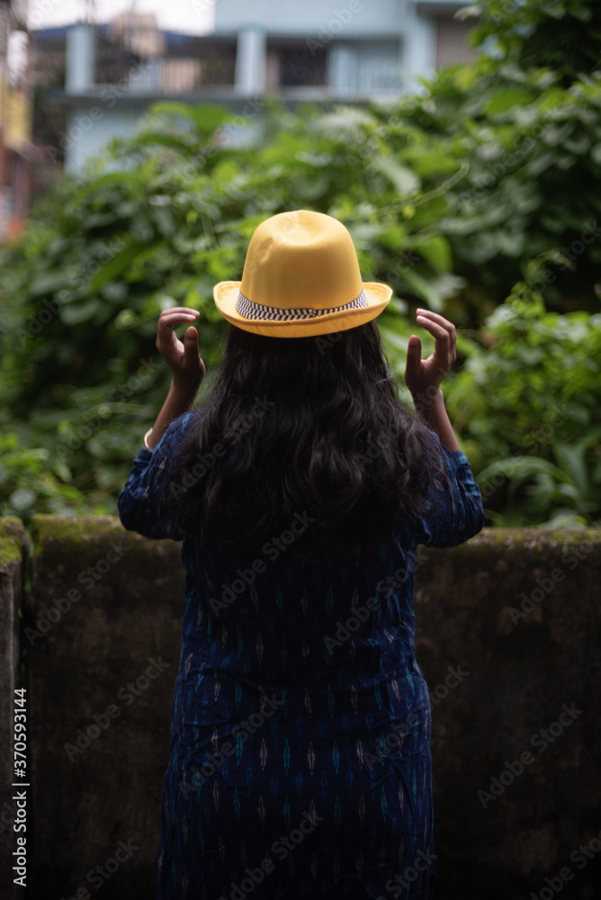 Backside view of an Indian woman standing in front of a green bush ...