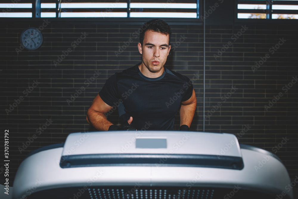 Fit man running in a gym on a treadmill looking to the screen ...