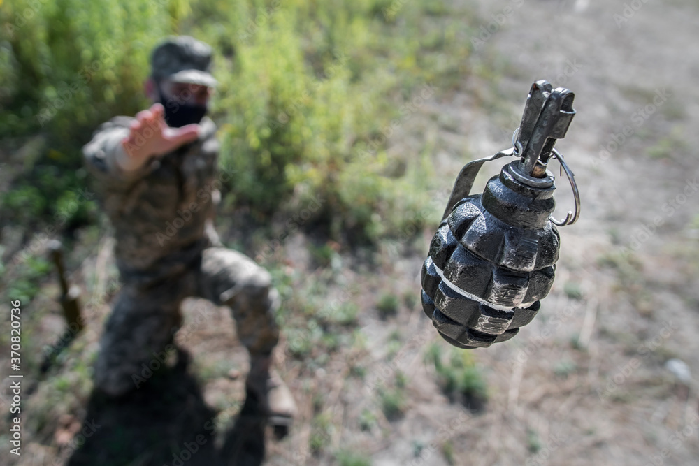 Grenade in flight with safety pin. A soldier in a mask threw a grenade ...