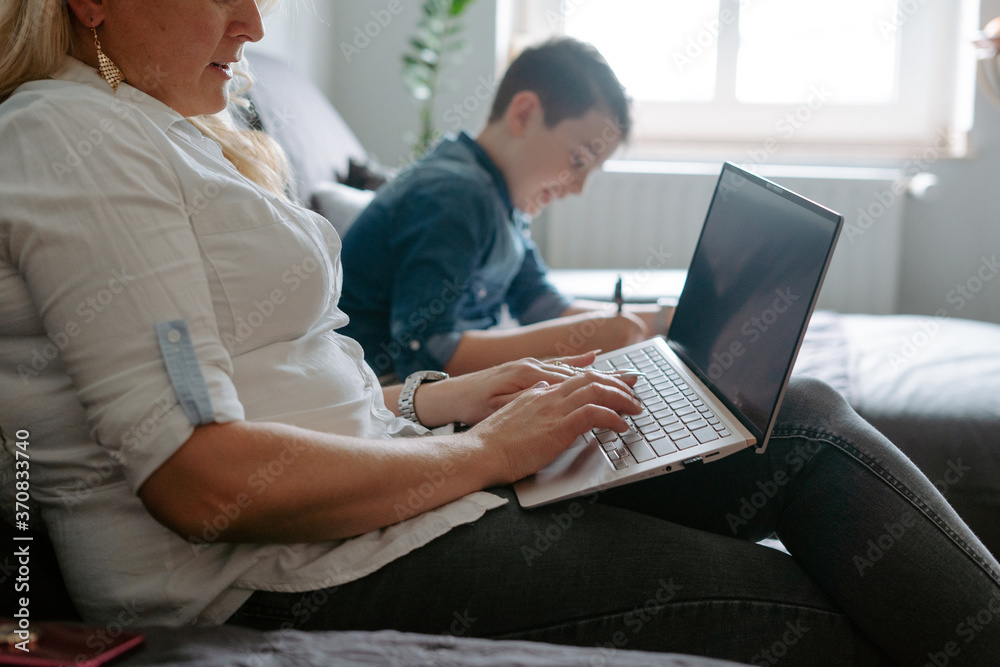Cropped mother using netbook while sitting near content son with sheet ...