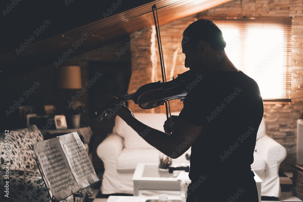 Side view of silhouette of male musician playing violin and looking at ...