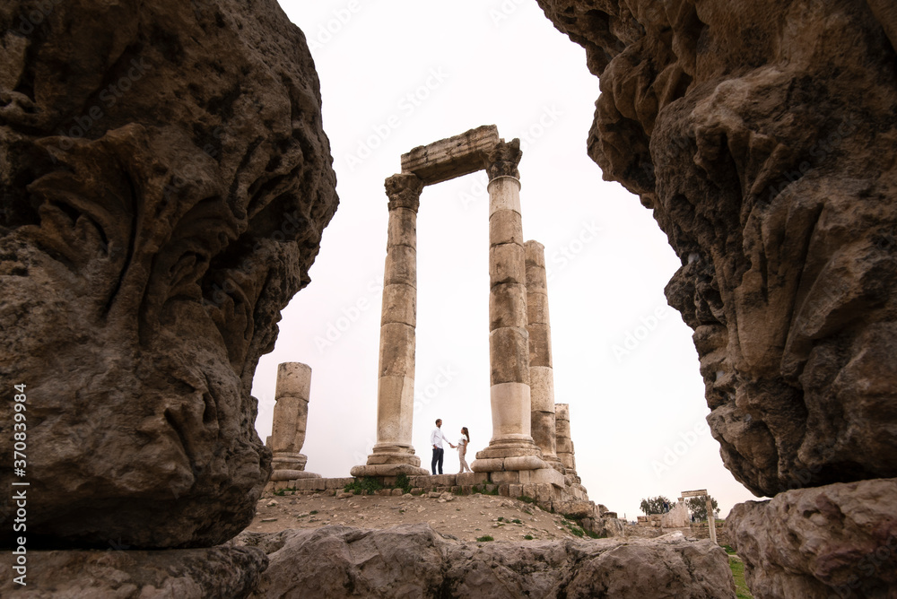 Tender couple of tourists standing under stone arch of Amman Citadel ...