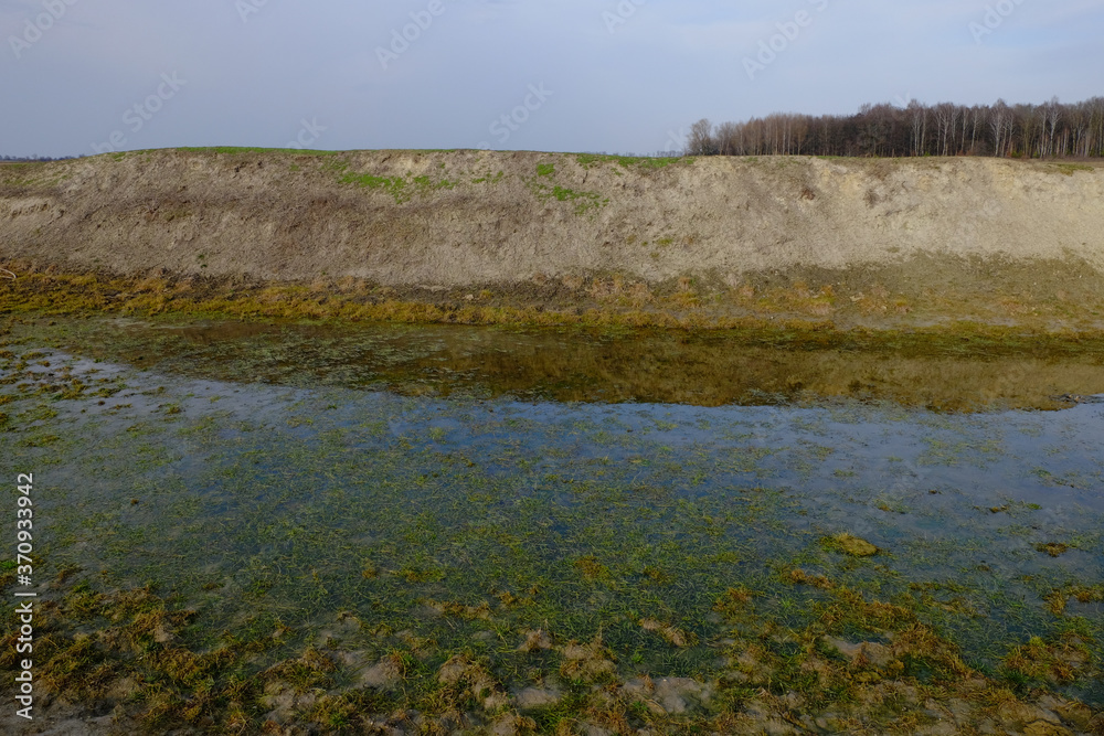 The exposed bottom of a dry pond. A shallow water body. A steep slope ...