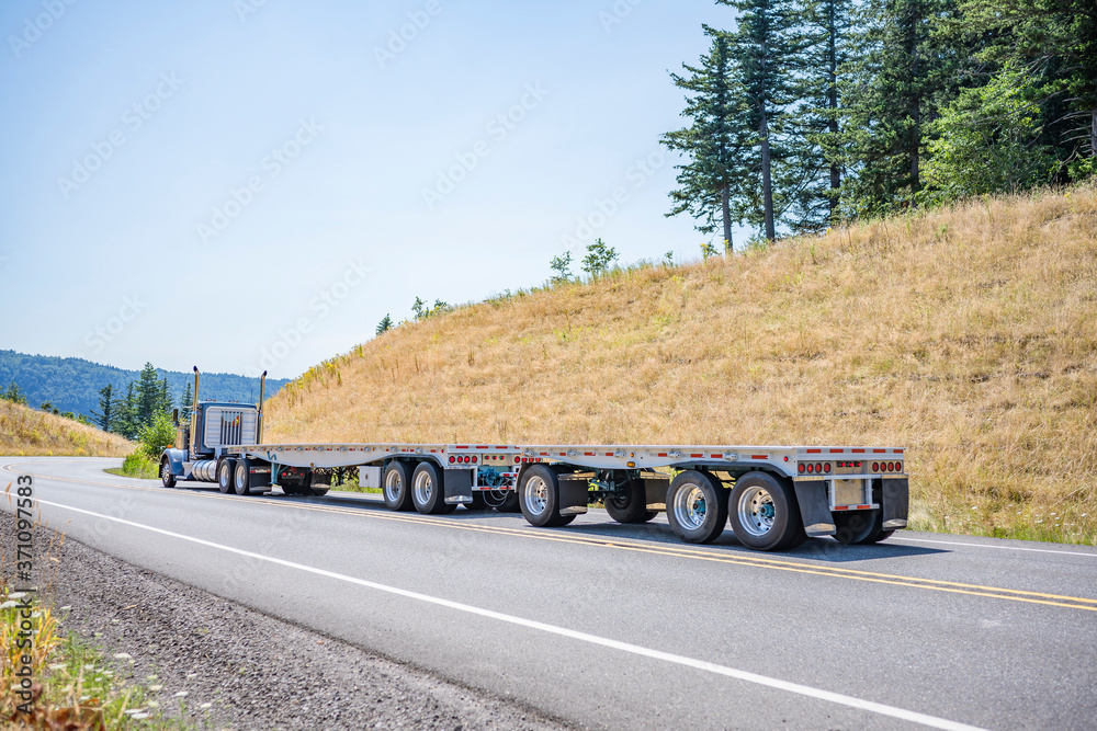 Blue big rig day cab semi truck tractor transporting two empty flat bed ...