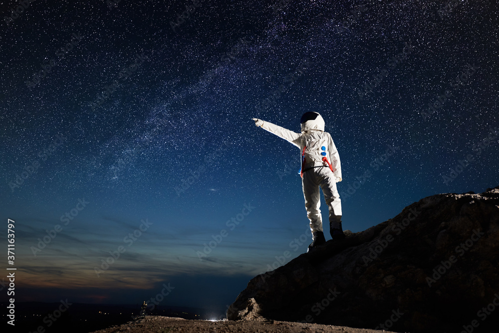 Full length of cosmonaut standing on top of rocky hill and pointing at ...