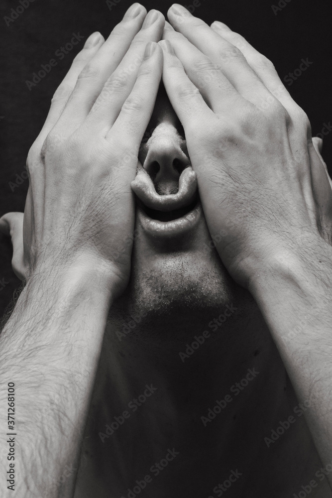 Monochrome portrait of a man deforms his face with his hands covering ...