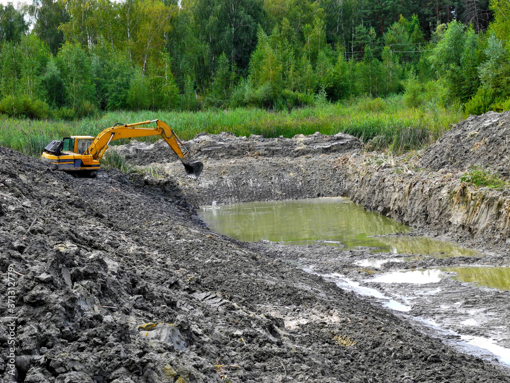 Foto de Excavator digging pond in forest. Clay soil in the foreground ...