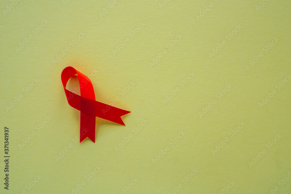 red loop ribbon as symbol of fighting cancer illness on clean yellow ...