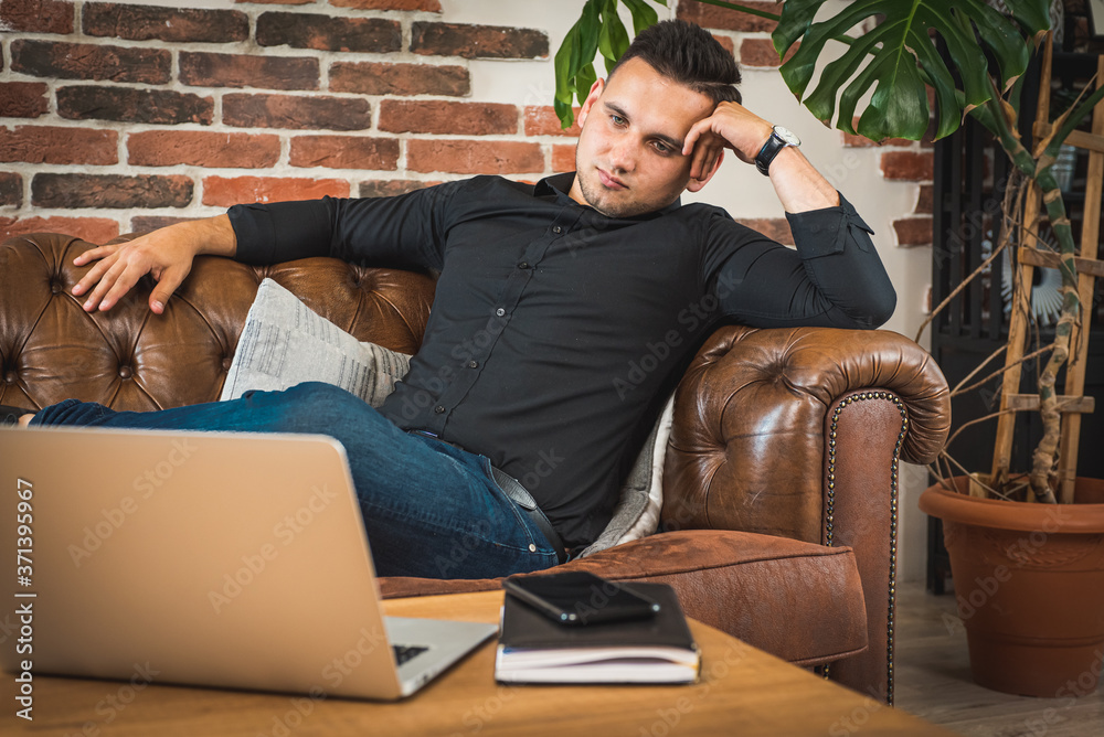 Multitasking. A handsome guy in a black shirt and jeans is lying on the ...