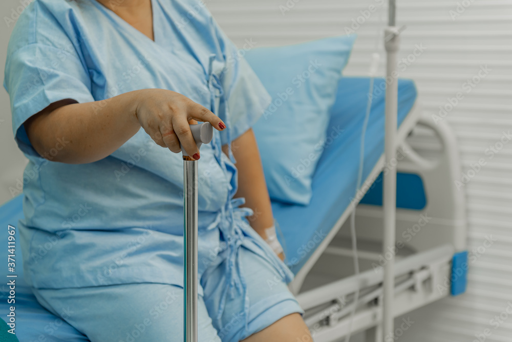 Overweight woman sitting on the bed with a cane in hospital. Stock ...