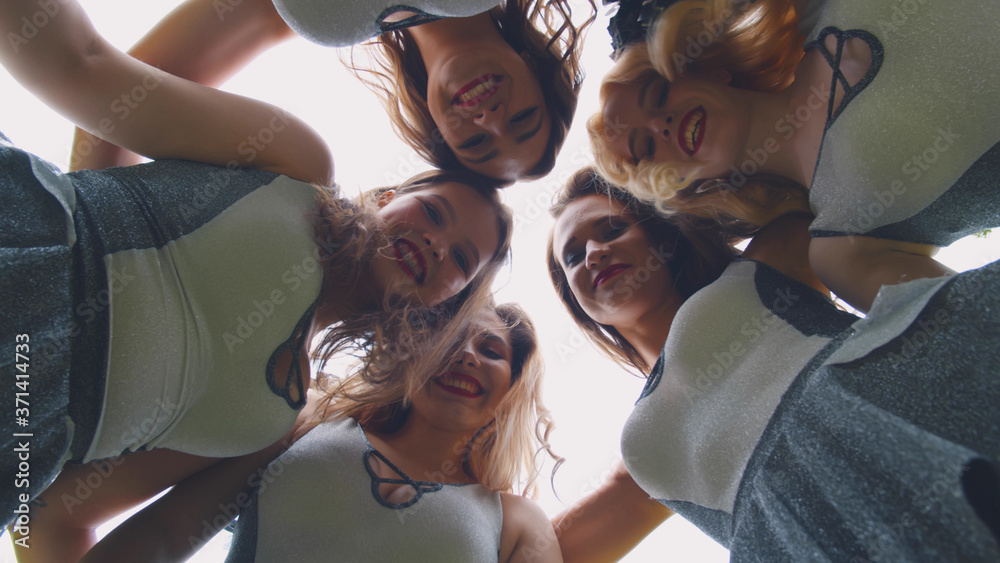 Bottom view of smiling cheerleaders hugging in circle and looking down ...