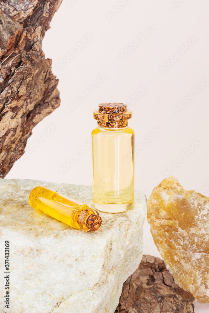 A bottle of natural essential oil on a stone, next to a tree bark with ...