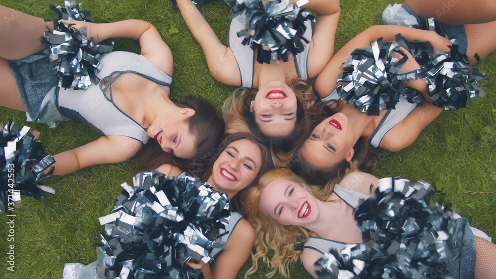 Top view of happy cheerleaders lying down on grass in circle and ...